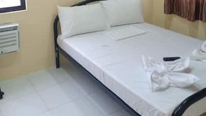 Uma cama de solteiro com roupa de cama branca, uma janela com persianas, um radiador e uma cortina na parede.