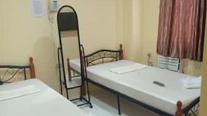 Quarto de estudante com duas camas de solteiro, um espelho, um telefone e uma cortina.