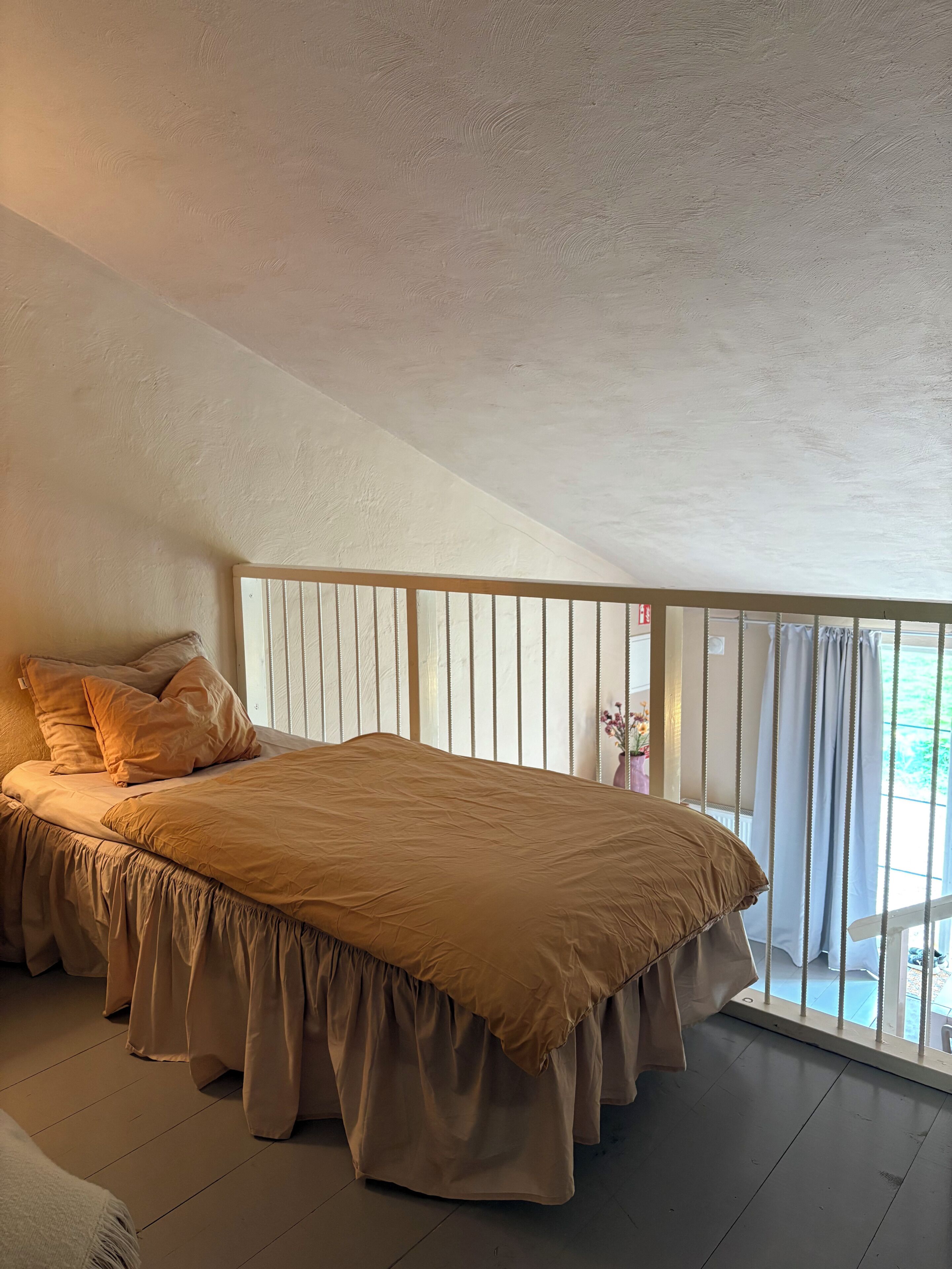Quarto com uma cama grande, varanda com guarda-corpo e vista para o exterior.