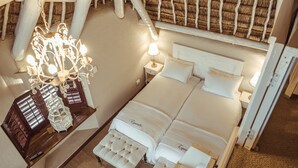 Quarto de hotel com cama, mesas de cabeceira, um candelabro e uma gaiola decorativa.