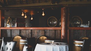 Um espaço de bar rústico com barris de madeira, poltronas de couro e luminárias pendentes.
