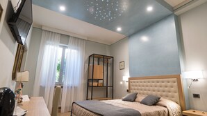 Quarto bem arrumado com cama, mesa de cabeceira e escrivaninha com cadeira.