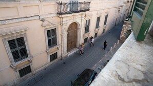 Uma rua estreita com edifícios em ambos os lados, destacando uma porta arqueada e uma varanda com grades de ferro forjado.