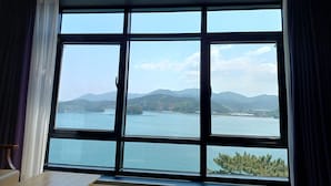 Quarto com uma grande janela que oferece vista para um lago e montanhas.