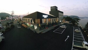 Hotel 'Bridge Hotel', com design moderno, estacionamento e vista para a água e colinas ao fundo.