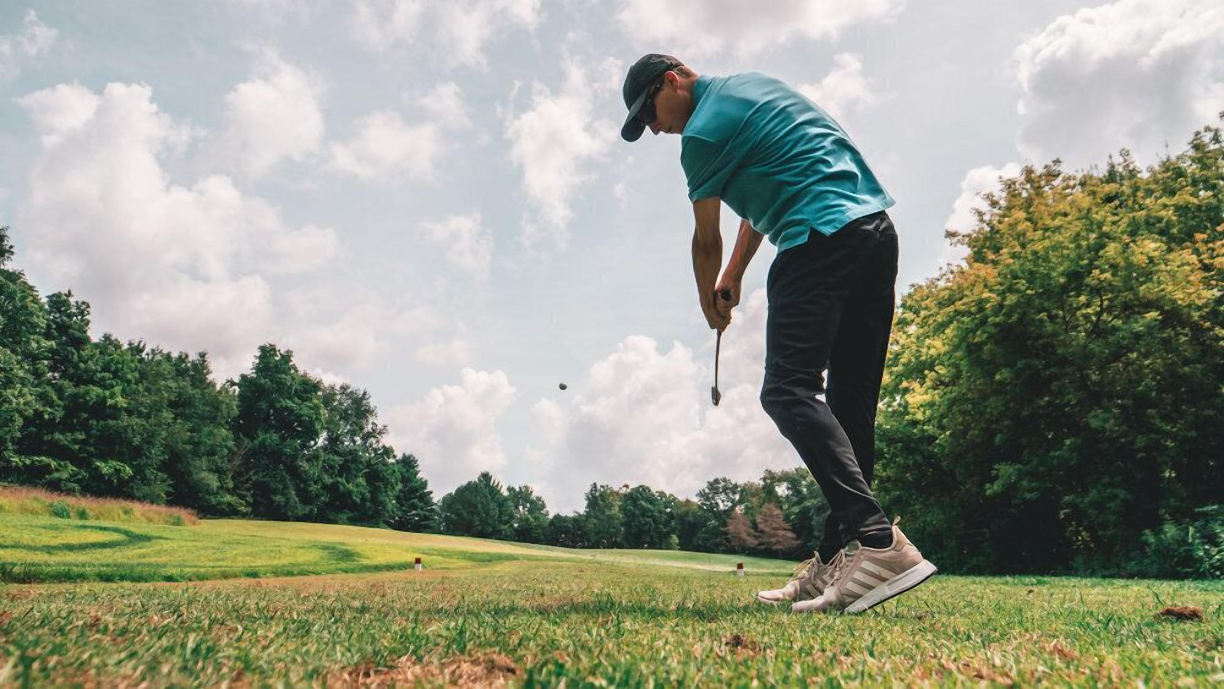 Uma pessoa vestida com camisa azul e calças pretas prestes a balançar um taco de golfe em um campo de golfe.