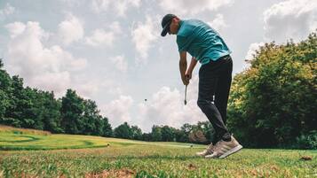 Uma pessoa vestida com camisa azul e calças pretas prestes a balançar um taco de golfe em um campo de golfe.