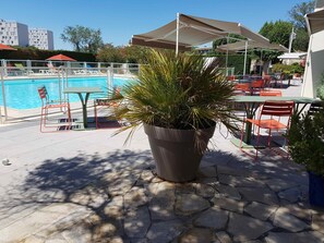 Uma área à beira da piscina com uma grande planta em vaso, espaço para sentar ao ar livre e vista para a piscina.