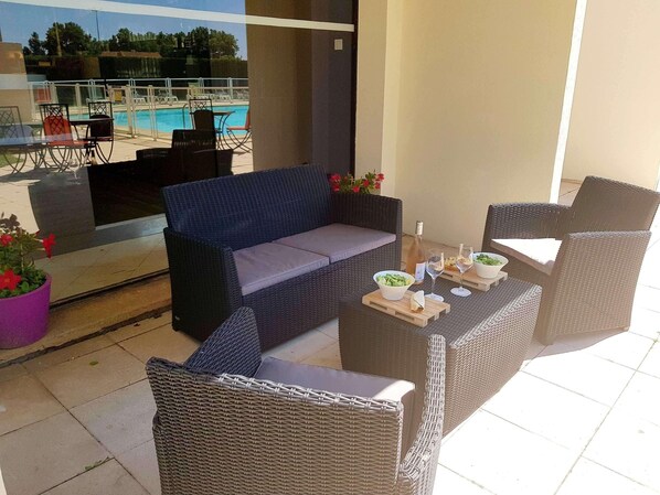 Área de pátio com mobiliário de vime, vista para a piscina e espaço para refeições ao ar livre.