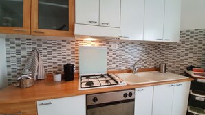 Uma cozinha compacta com armários brancos, fogão a gás, pia e lava-louças.