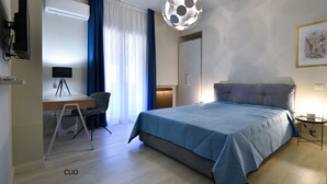 Quarto de hotel moderno com uma cama grande, uma mesa com cadeira, televisão e uma luminária de teto original.