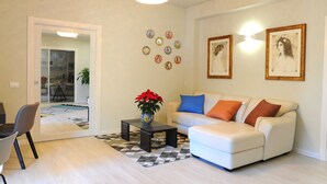 Uma sala de estar com um sofá branco, uma mesa de centro com um vaso de flores e um tapete estampado.
