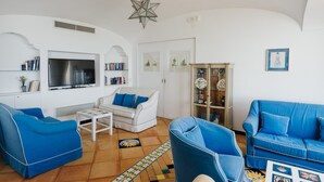 Uma sala de estar com sofá branco, poltronas azuis, mesa de centro, televisão e uma estrela decorativa pendurada no teto.