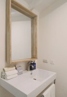 Casa de banho com lavatório branco, espelho com moldura de madeira e duas embalagens de sabonete líquido.