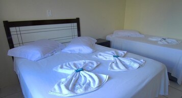 Quarto de hotel com duas camas, cada uma com lençóis e toalhas brancas dobradas em laço.