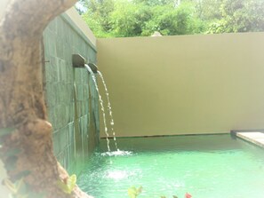 Piscina com cachoeira, rodeada por um muro de pedra e vegetação.