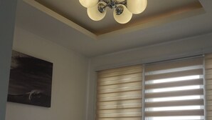 Uma sala de estar moderna com um sofá preto, luminária no teto e uma janela grande com persianas.
