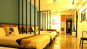 Quarto de hotel com três camas, uma televisão e uma escrivaninha.