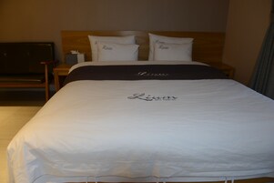 Cama bem arrumada com colcha branca e dois travesseiros, cada um com a etiqueta 'Linum Spa Hostel'.