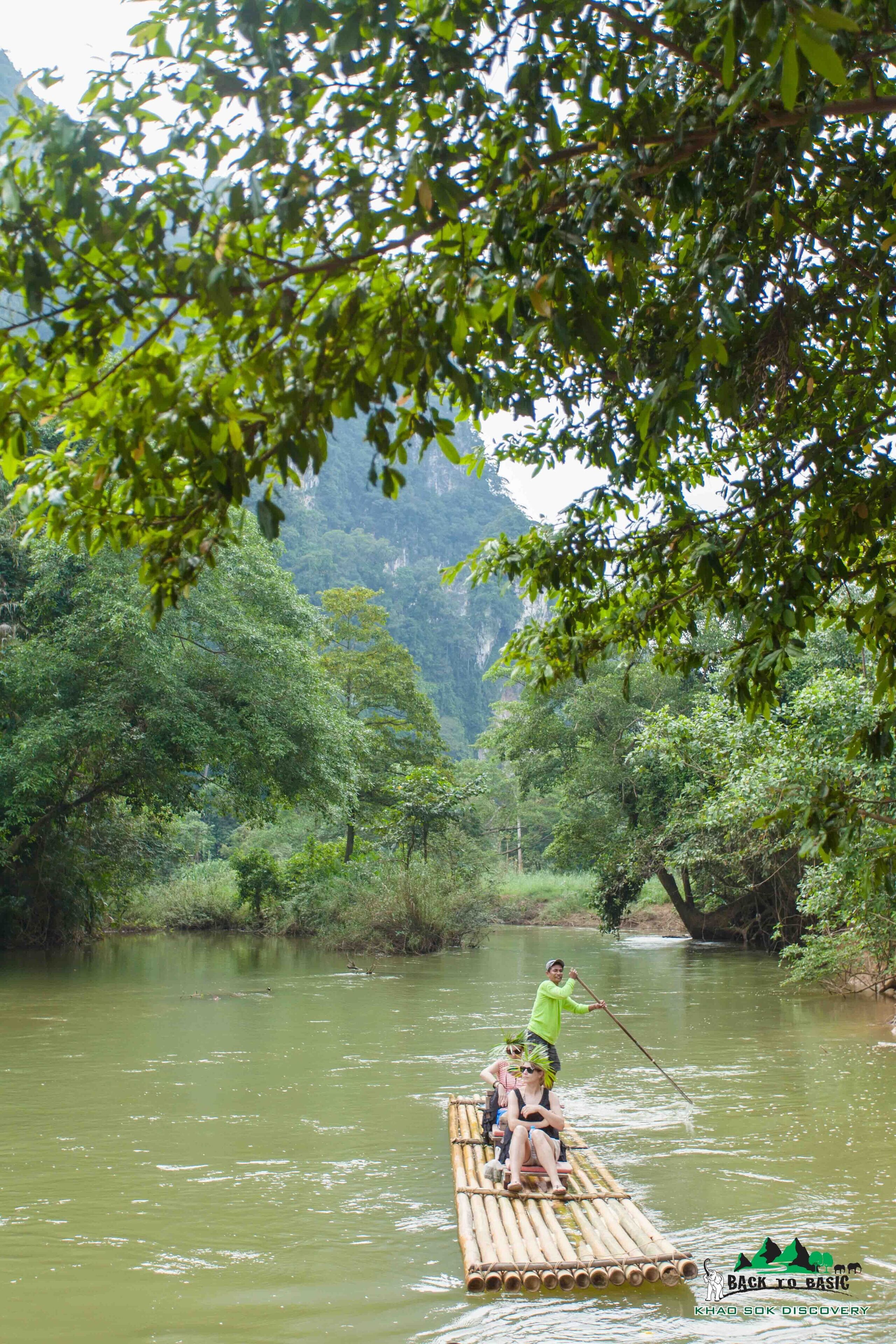 Uma jangada de bambu em um rio, cercada por vegetação densa e montanhas.