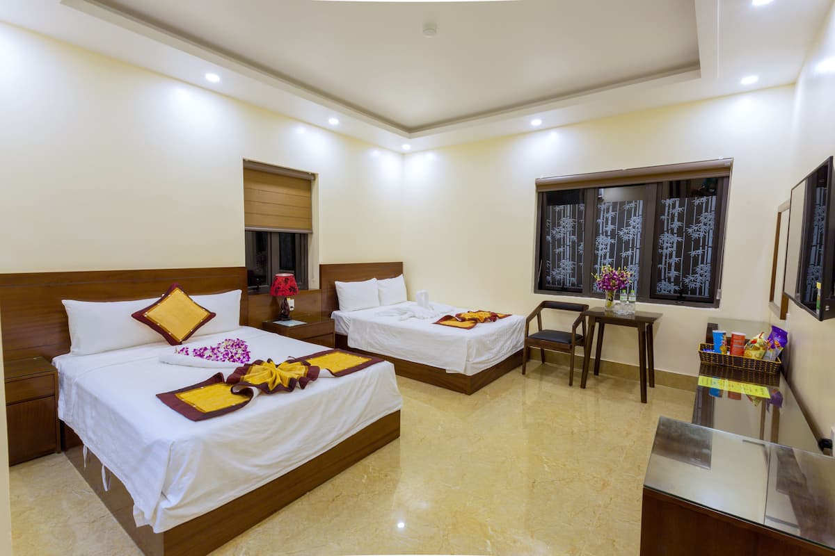 Quarto de hotel com duas camas, uma escrivaninha, uma cadeira e uma mesinha de centro com um vaso de flores.