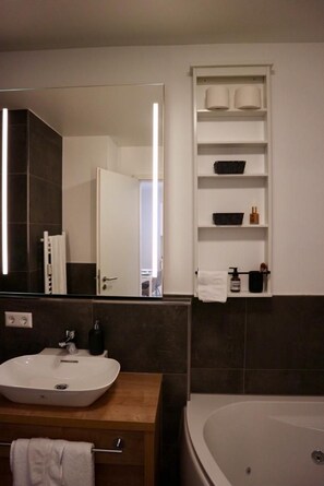 Uma casa de banho moderna com uma pia branca, um espelho grande, uma banheira e um armário embutido com artigos de higiene pessoal.