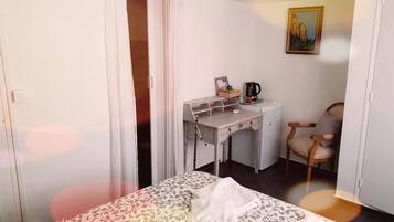 Um quarto pequeno e bem iluminado, com uma cama, uma escrivaninha e uma cadeira.