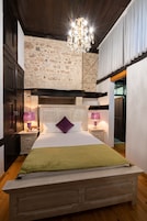 Quarto com cama grande, piso de madeira, parede de pedra e um candelabro.