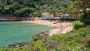 Uma área costeira com praia, águas cristalinas e edifícios ao fundo.