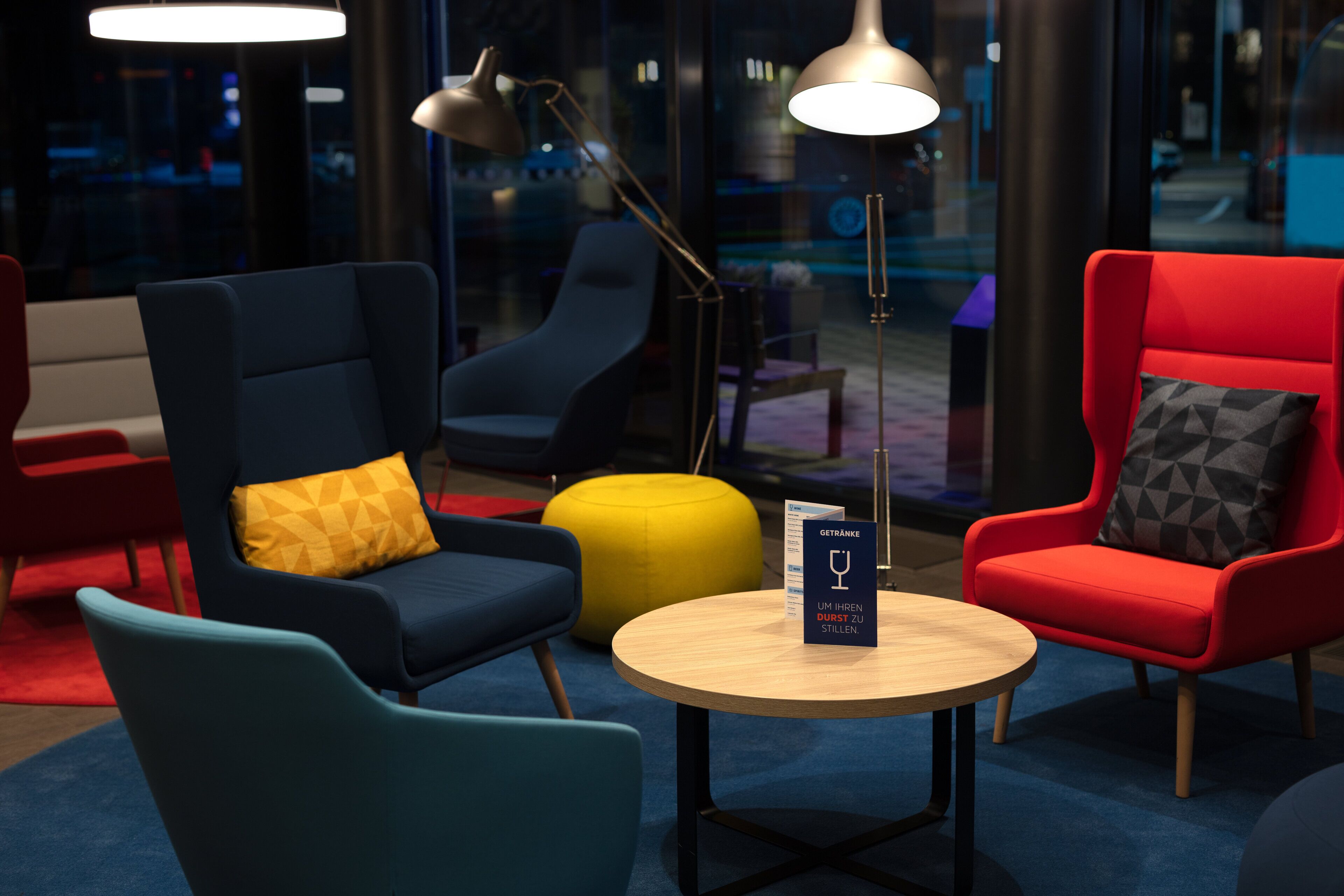 Uma área de estar moderna com assentos confortáveis, uma mesa redonda e um porta-livros.