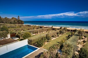 Piscina com deck de madeira, cercada por jardins bem cuidados e vista para o oceano.