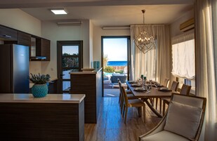 Cozinha moderna com vista para o mar, sala de jantar com mesa posta para quatro e varanda com mobiliário de exterior.