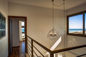 Uma escadaria com vista para a praia, um lustre pendurado e uma porta que dá para outro cômodo.