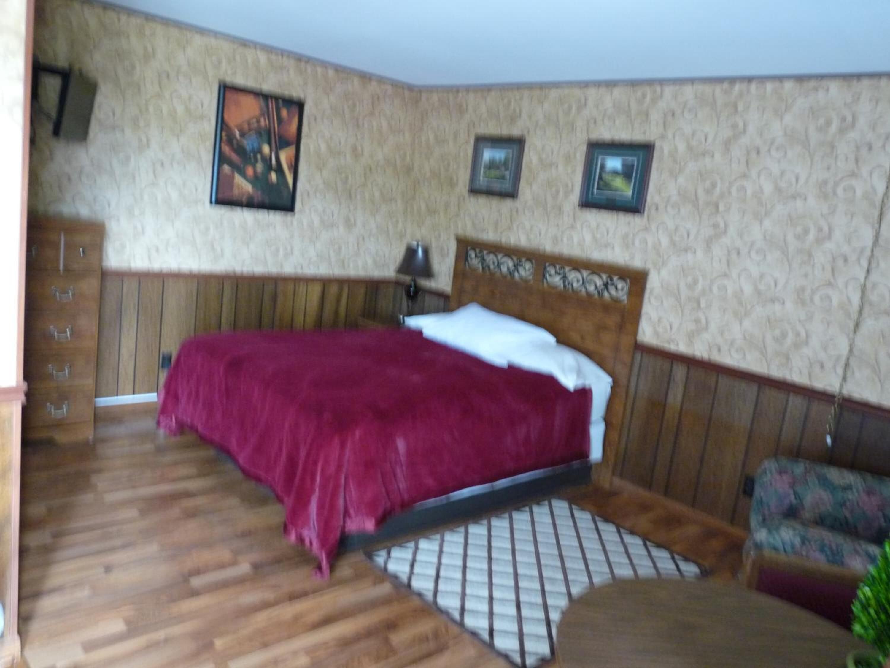 Quarto com cama de madeira, cômoda de madeira, parede estampada e pequena mesa com cadeira.