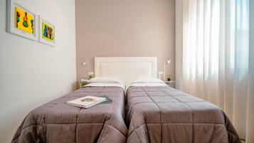 Uma cama de casal com cabeceira, duas mesas de cabeceira e uma janela com cortinas.