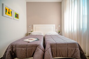 Uma cama de casal com cabeceira, duas mesas de cabeceira e uma janela com cortinas.