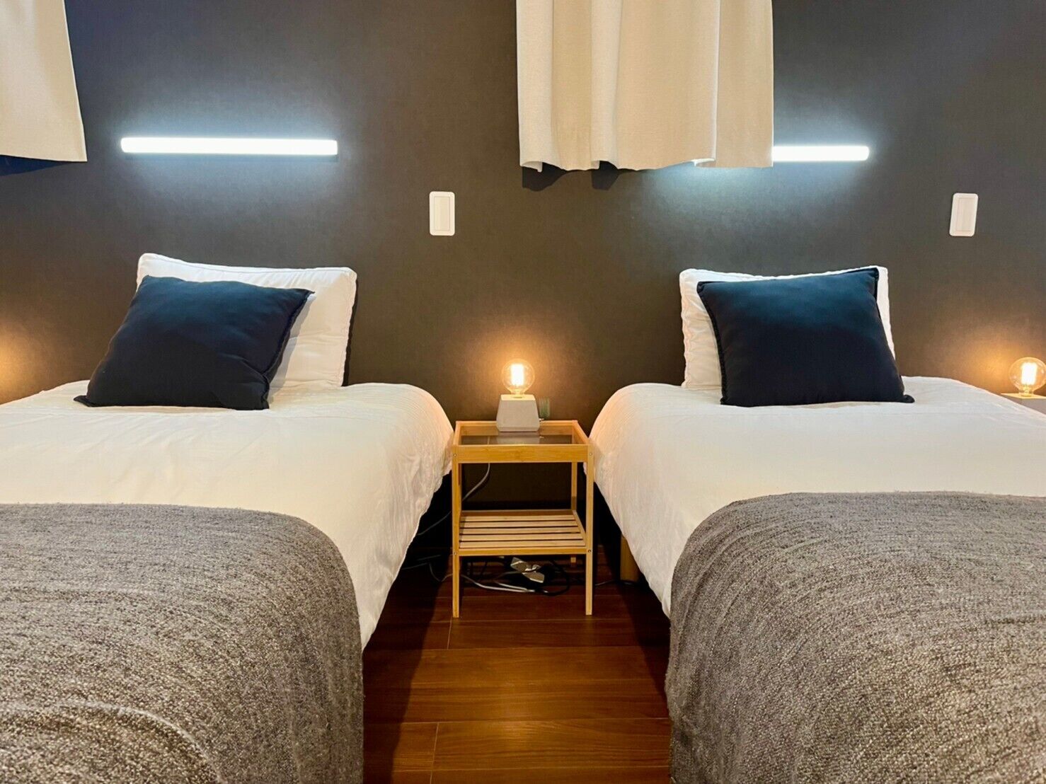 Quarto de hotel com duas camas, cada uma com travesseiro e mesa de cabeceira com abajur.
