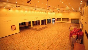Um salão amplo com piso estampado, ventiladores no teto e fileiras de cadeiras ao longo das paredes.