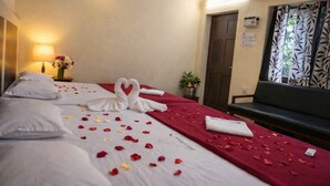 Quarto de hotel com duas camas, um cobreleite vermelho e uma toalha disposta em formato de coração em uma das camas.