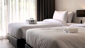 Quarto de hotel com duas camas, uma mesa de cabeceira com abajur e uma janela com cortinas.