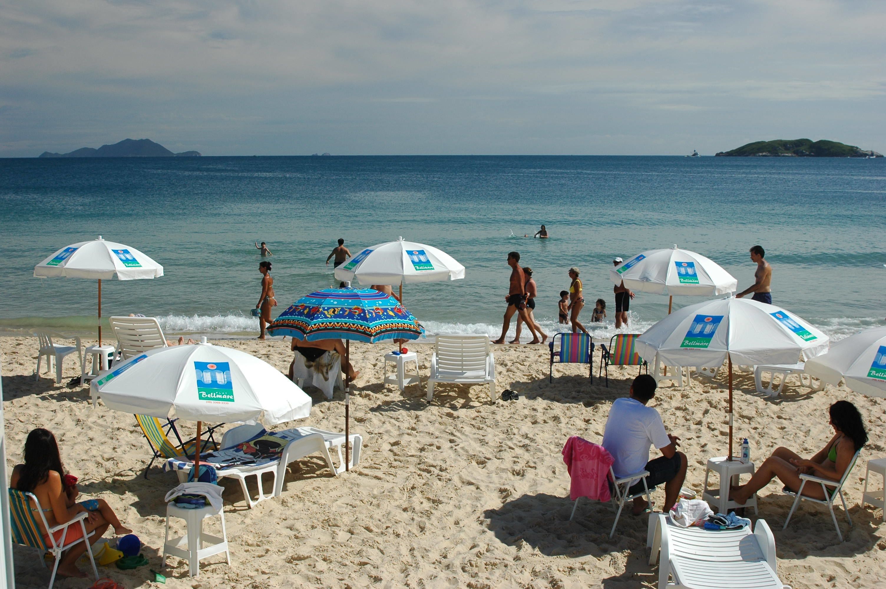 Uma praia com vários guarda-sóis brancos e espreguiçadeiras.