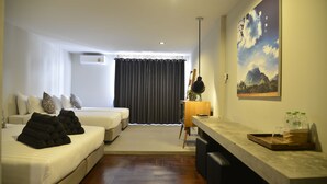 Quarto de hotel moderno com cama, sofá, escrivaninha e uma janela grande com cortinas.