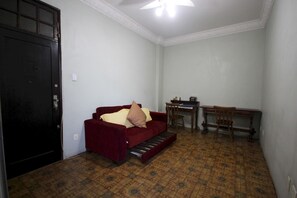 Quarto com sofá vermelho, escrivaninha de madeira e piso estampado.