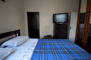 Quarto com cama, televisão sobre suporte, guarda-roupa e porta.