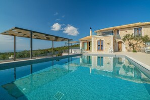 Uma piscina com pérgola, uma casa de pedra com varanda e vista para a paisagem.