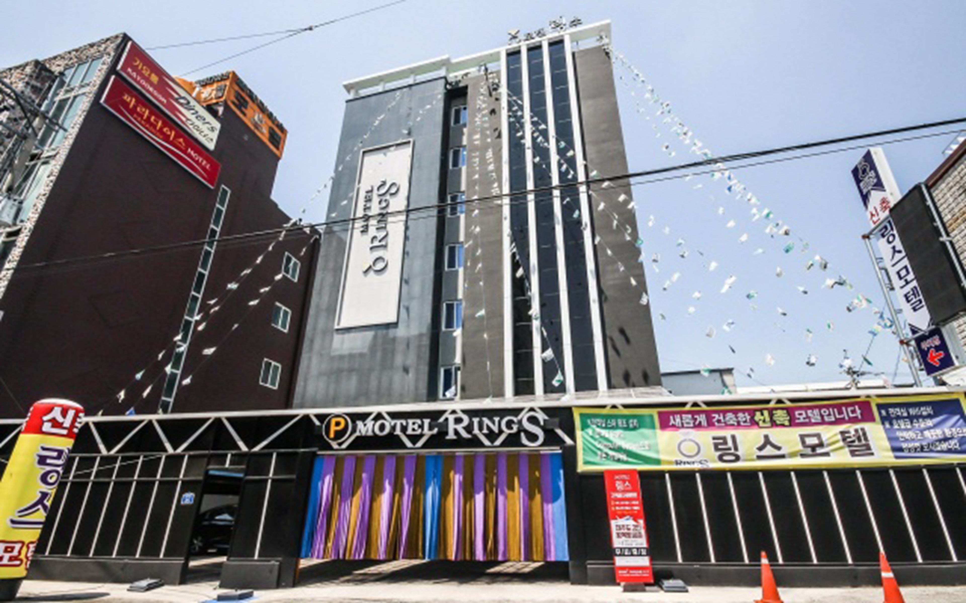 Um edifício com uma placa que diz 'Motel Rings' e uma grande placa vertical com texto em coreano.