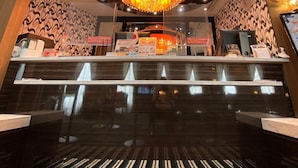 Uma área de recepção de hotel com um lustre moderno, balcão de recepção e paredes com padrão.
