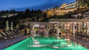 Piscina com espreguiçadeiras, área de bar e vista para um morro com edifícios.