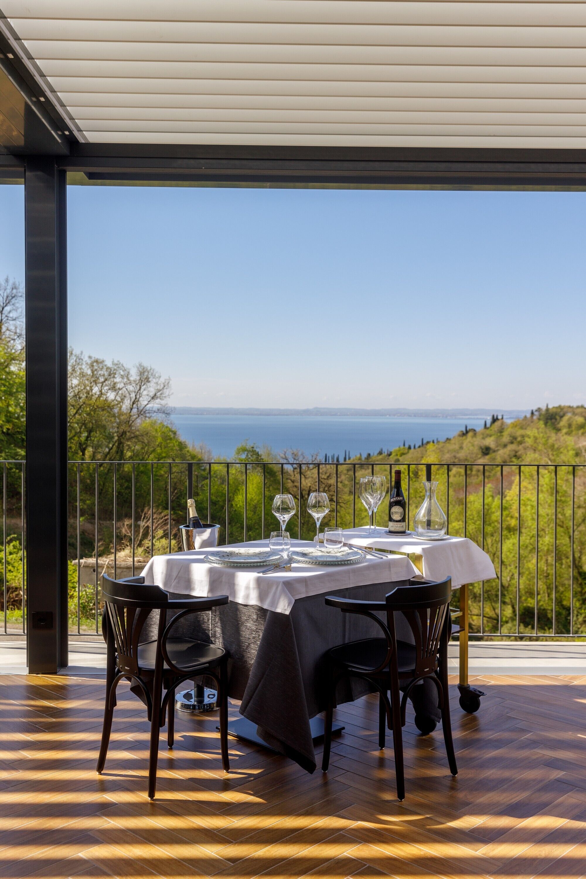 Uma área de refeições ao ar livre com uma mesa posta para dois, com vista para o mar e colinas.