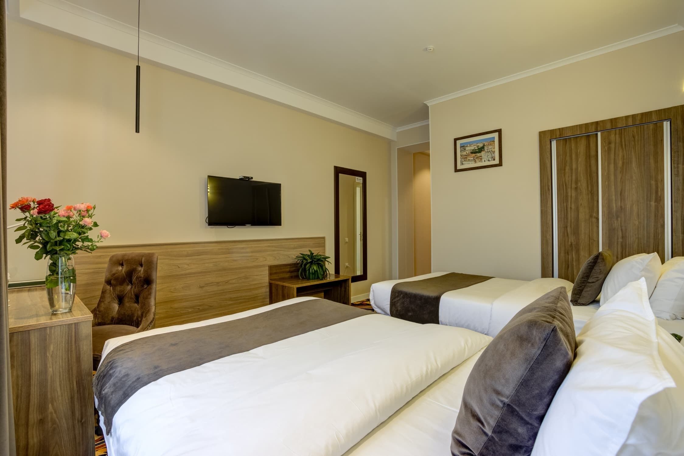 Quarto de hotel com duas camas, televisão, espelho e cabeceira de madeira.